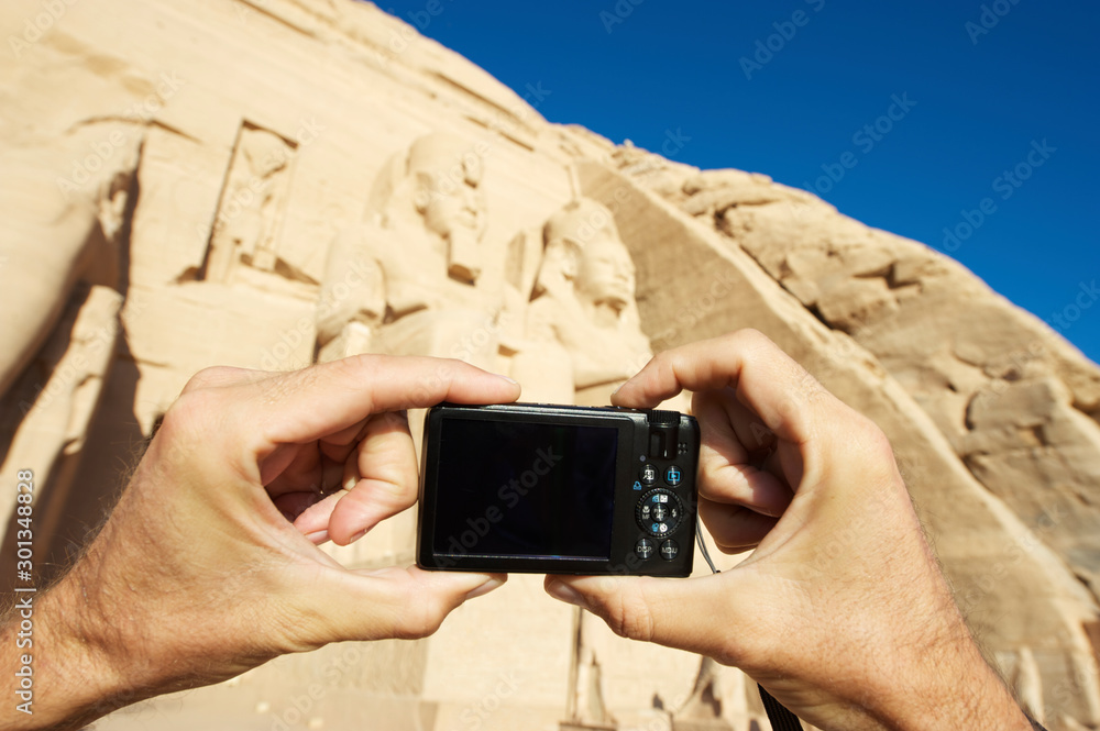 Tourist hands holding a small camera pointing at the row of Ramses ...
