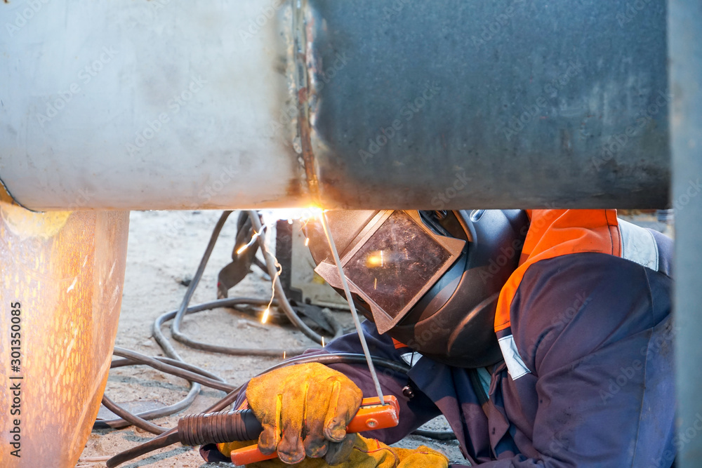 Manual arc welding. A professional welder welds a pipe with a diameter ...