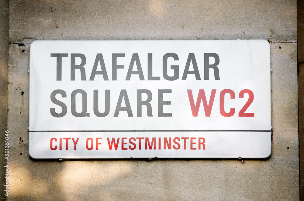 Light reflects on the stone wall holding up a street sign for Trafalgar ...