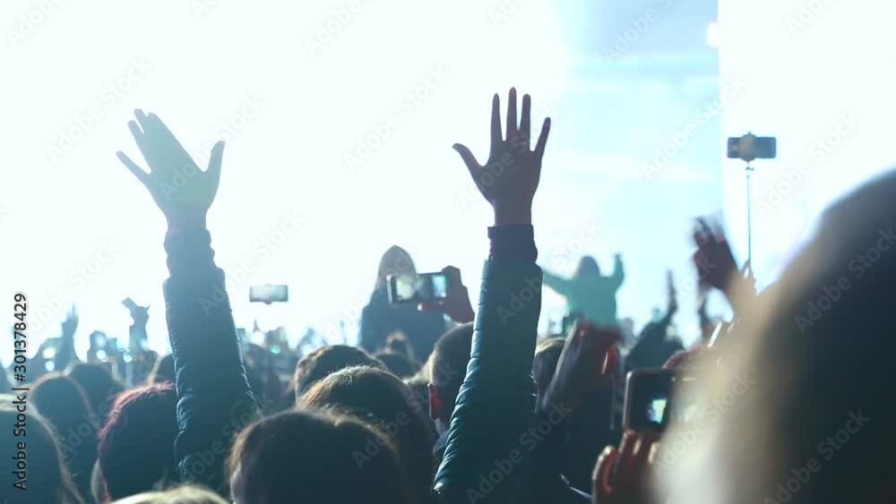 Crowd of spectators raises their hands up and applauds the musician ...
