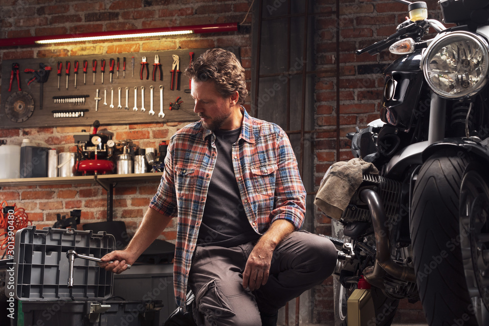 Biker or mechanic working on his vintage motorcycle in a workshop with ...