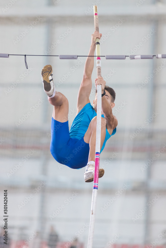 Poster Pole vaulting indoors - young man jumping over the partition ...