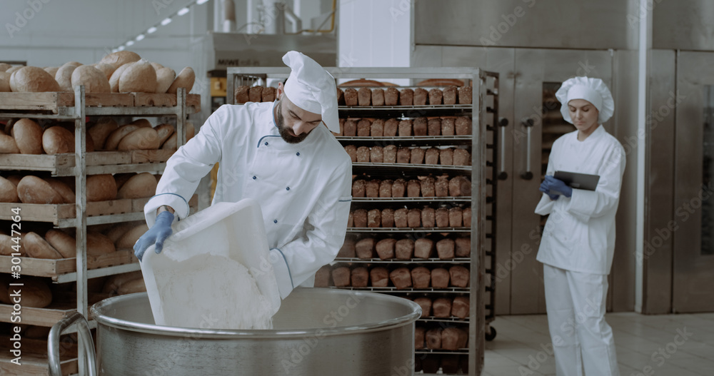 Bakery industry big chef in a special uniform preparing the dough add ...