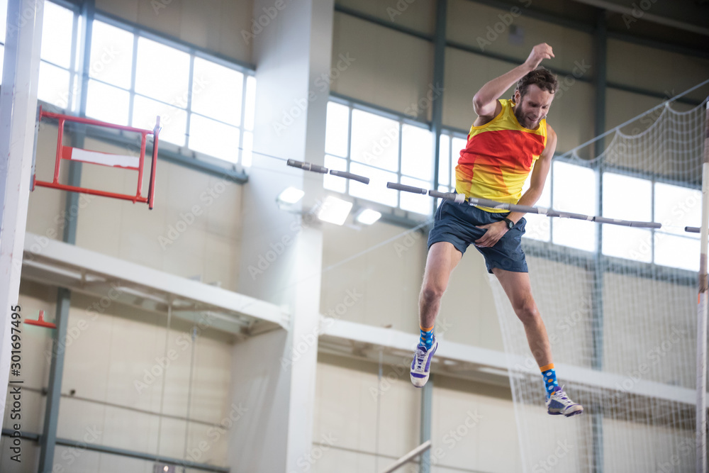 Pole vaulting indoors - a athletic man jumping over the bar and trying ...