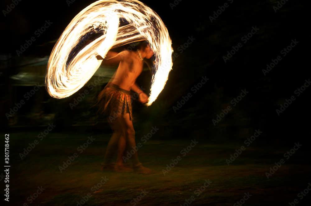 Unrecognizable shirtless male fire dancer twirling flaming torches at ...