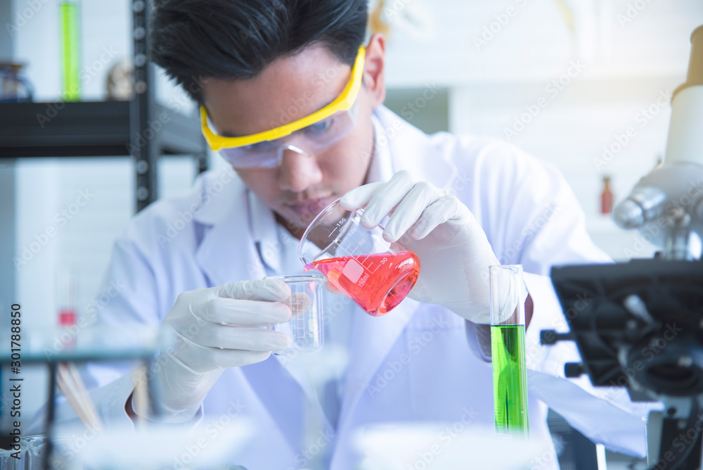 Asian young scientist is researching the experiment to pour chemicals ...
