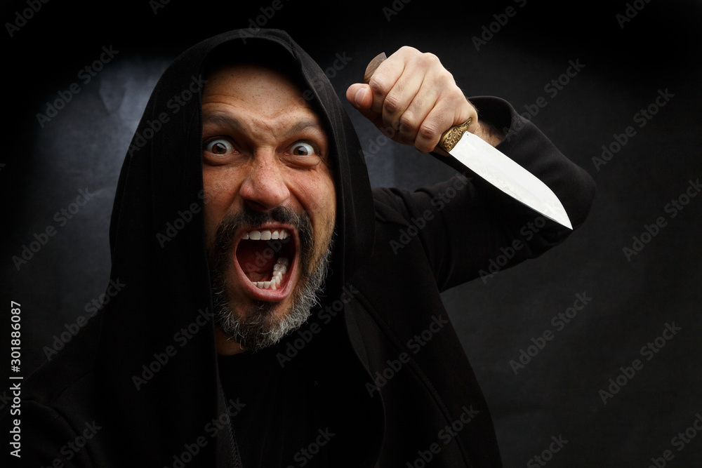Portrait of a bald man with a beard in a black hood with a knife on a ...