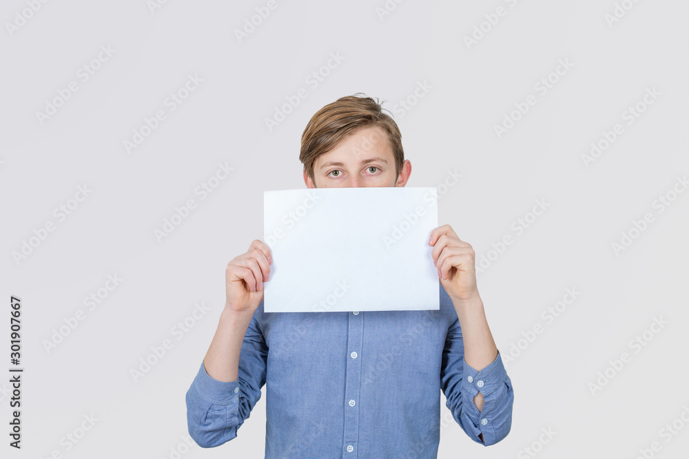 Teenage boy covering his face with a empty white paperT over white ...