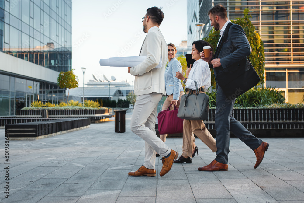 Group of coworkers walking outside in front of office buildings discuss ...