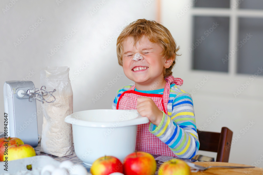 Cute little happy blond preschool kid boy baking apple cake and muffins ...