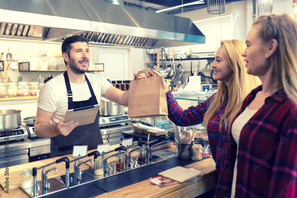 Waiter serving takeaway food to customers at counter in small family ...