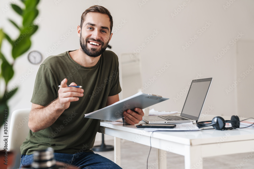 Image of smiling young man pointing finger at camera and holding ...