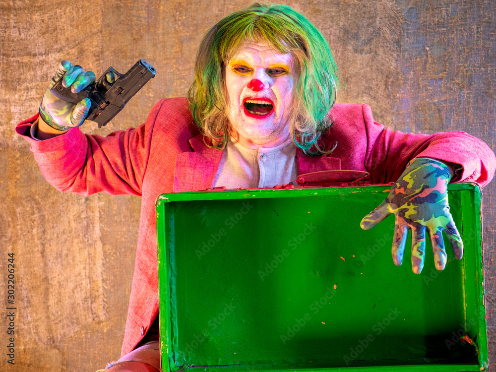 Evil clown with gun and pink green suitcase. man hates his work and in ...