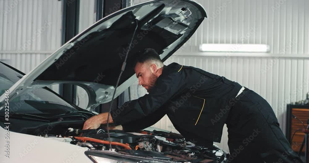 Sweating mechanic guy in a garage working very concentrated over a car ...