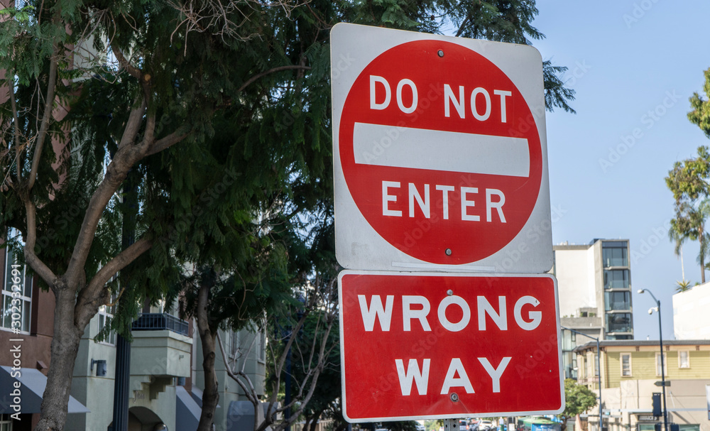 Do Not Enter Wrong Way street sign with trees and houses in the ...