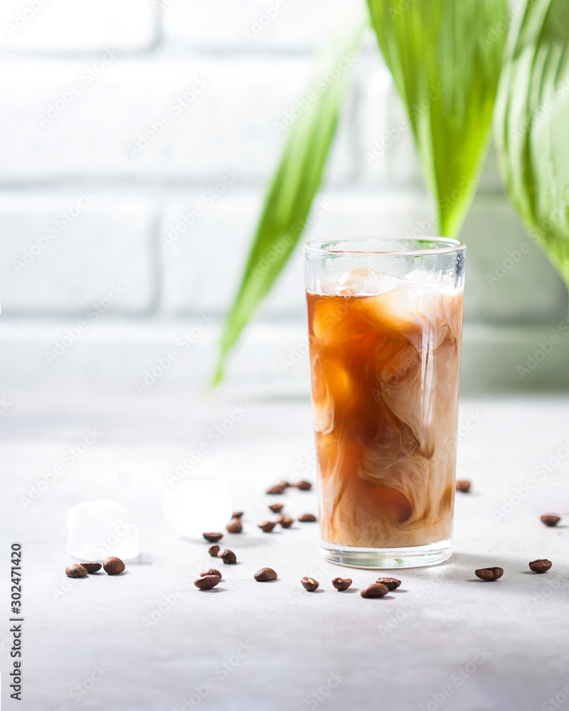 Cold brewed iced coffee in a tall glass cup and coffee beans on a gray ...