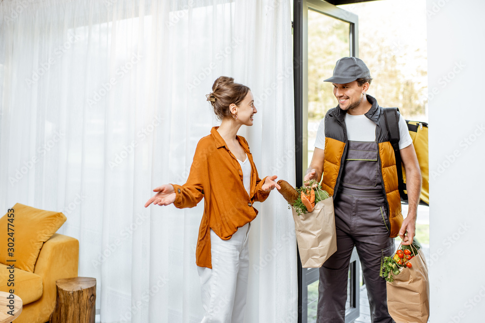 Courier in uniform delivering fresh groceries home for a young client ...