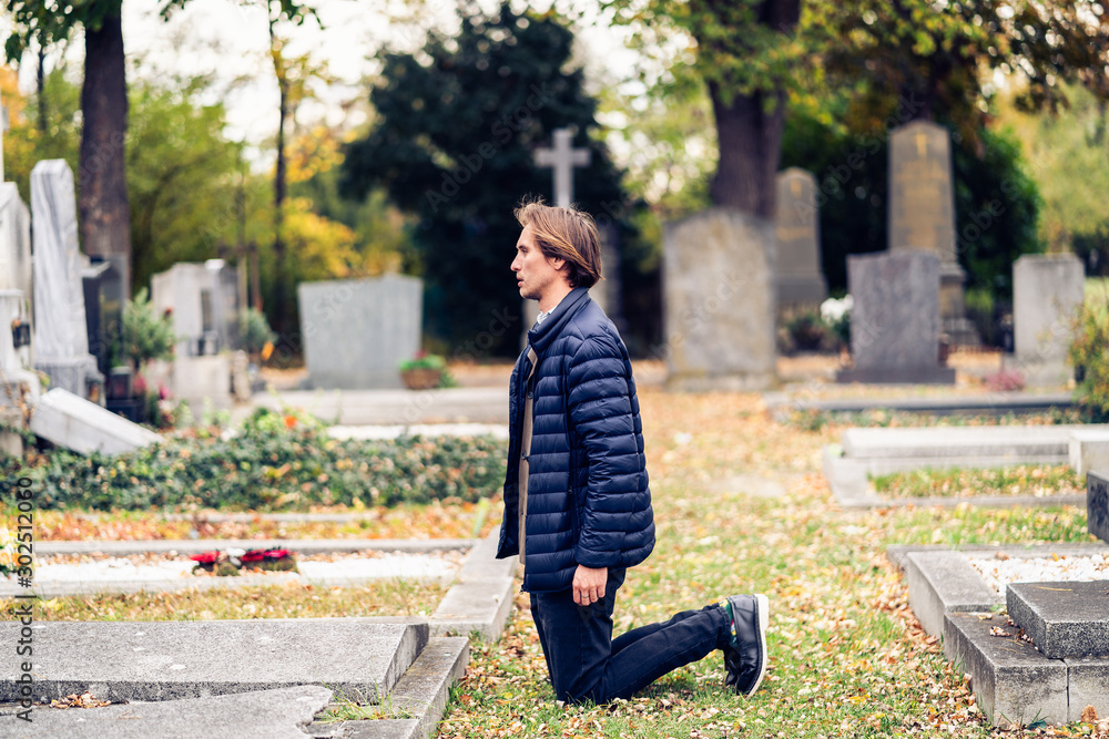 Mourning young man kneeling in front of a grave on a cemetery Stock ...