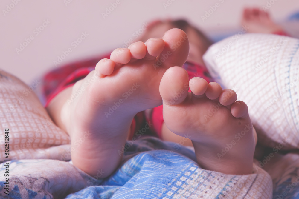Little child girl sleeping in bed at home. Feet under the blanket on ...