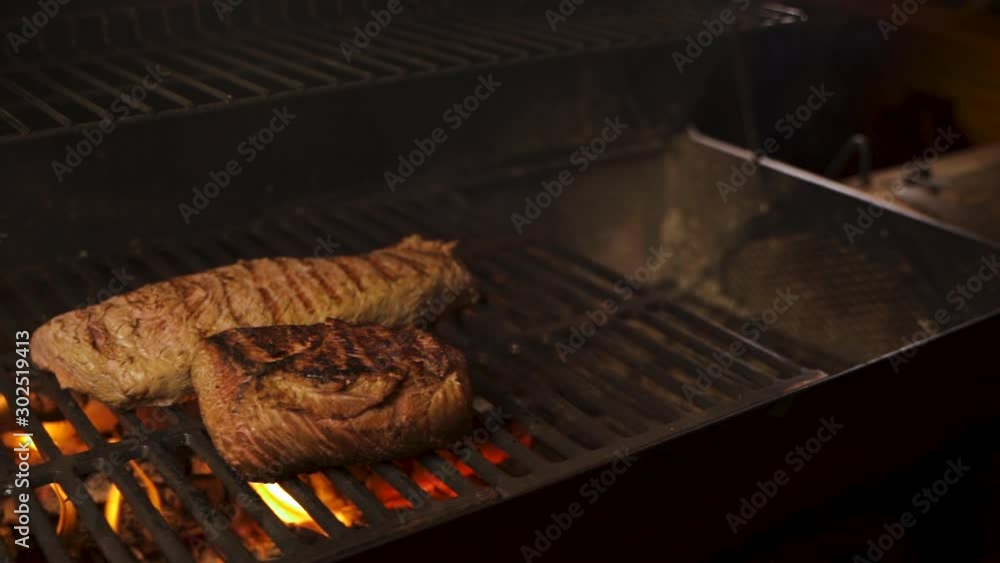 Chef opens BBQ Smoker where steaks of pork beef meat cooked on fire ...