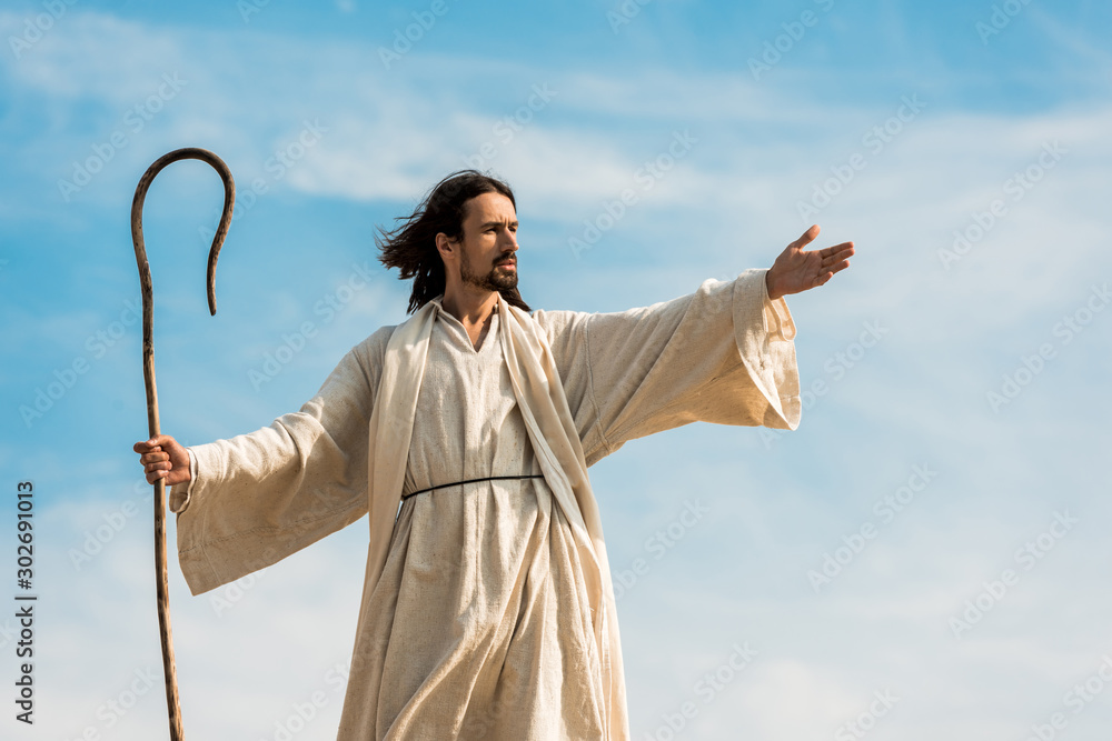 Jesus with outstretched hand holding wooden cane against blue sky foto ...