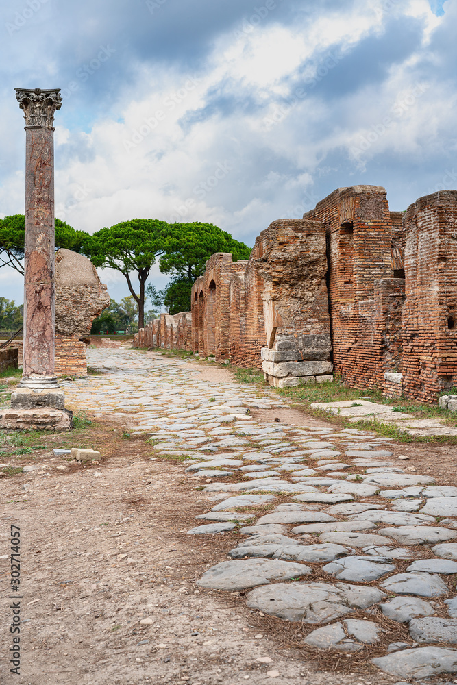 Old narrow stone road in the Italian antique city of Ostia Antica among ...