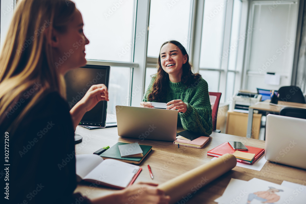 Smiling young women having fun during cooperation at desktop in office ...