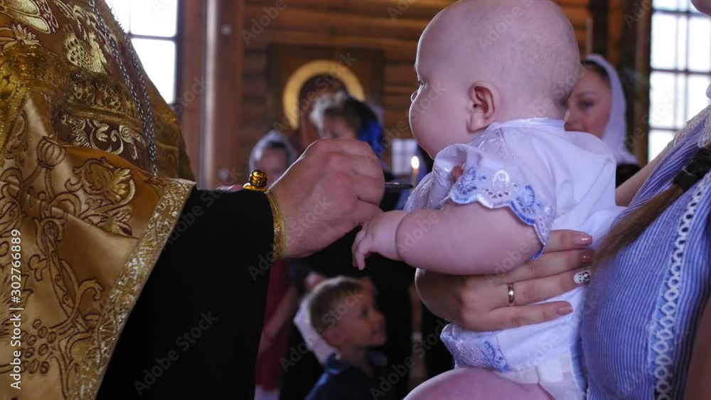 Baby boy getting babtized at a christening. Mother holds chubby baby in ...