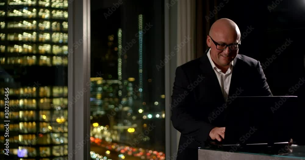 bald man in glasses and a suit is working merrily at a laptop near a ...