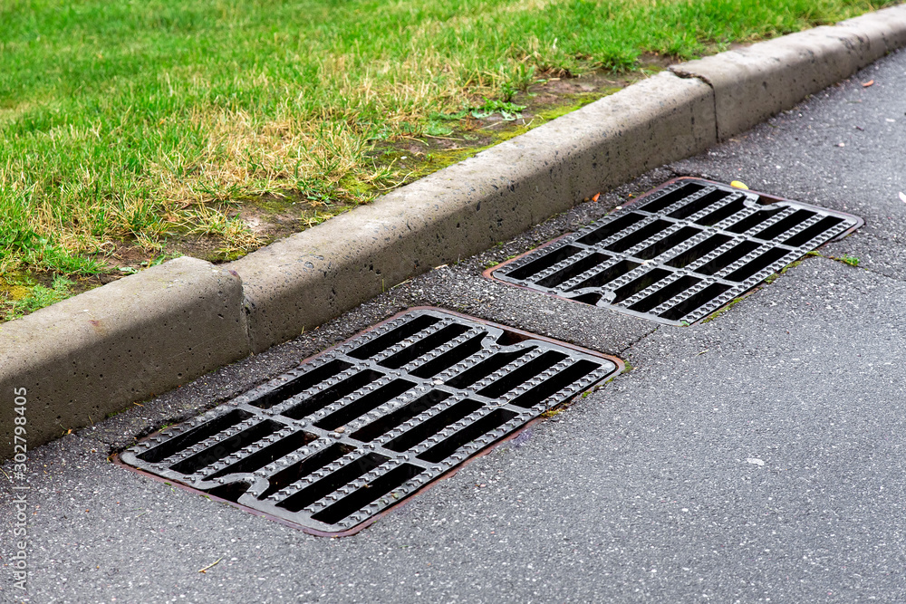 manhole cover rain grate on an asphalt road near a stone curb on the ...