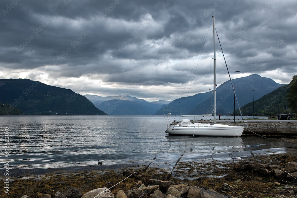 Mooring yacht in low tide in Norwegian fjord against dark cloudy sky ...