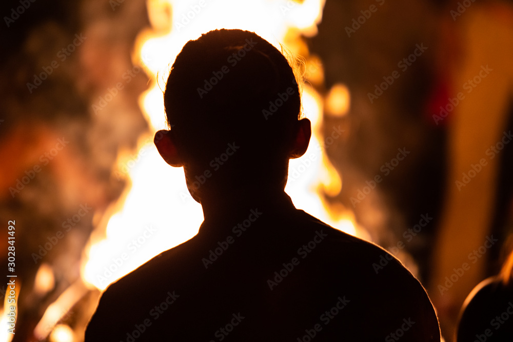 silhouette of an unrecognizable person sitting in the front of the fire ...