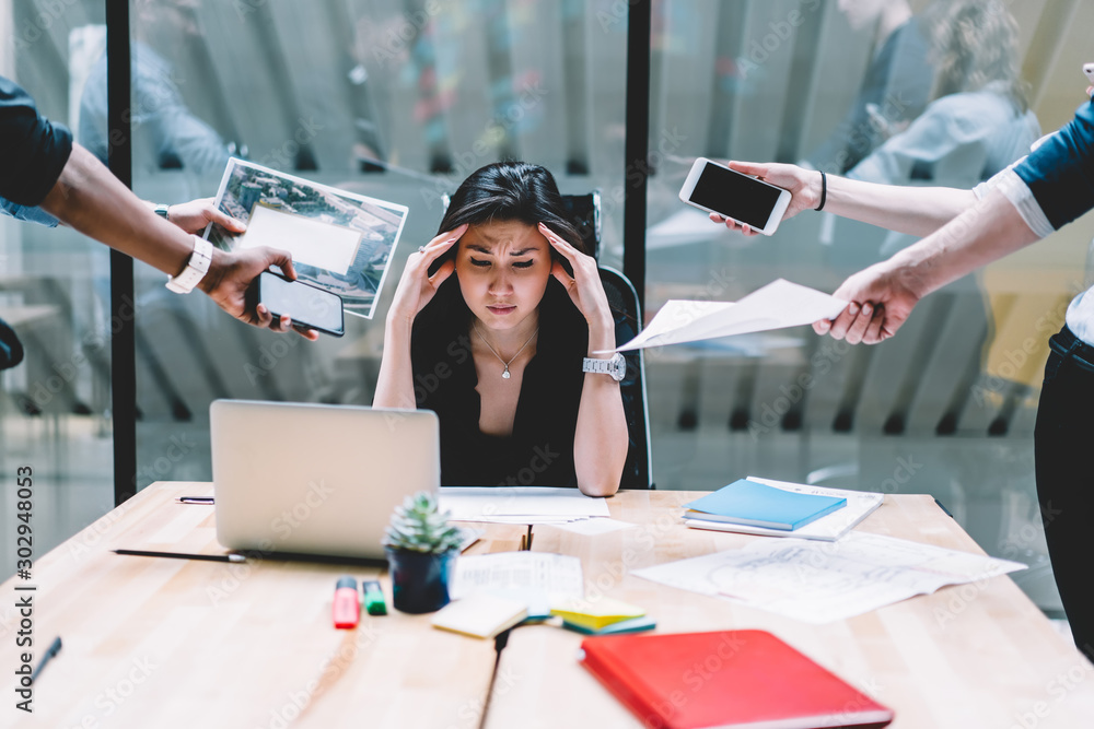 Young disappointed woman feeling headache from deadline surrounded by ...