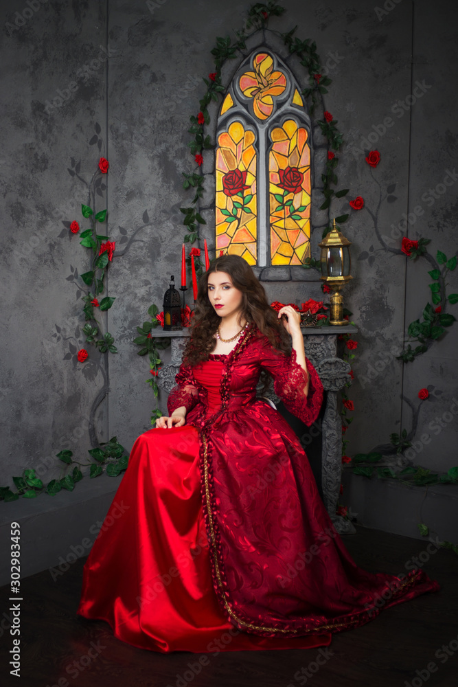 A beautiful girl in a magnificent red dress of the Rococo era sits on a ...