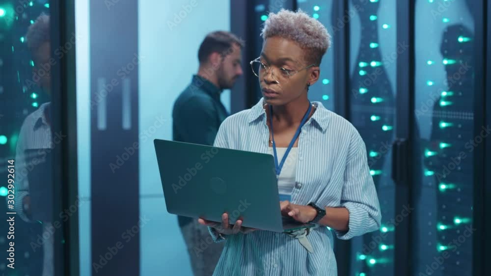 Black female IT engineer upgrading hardware in rack server room ...