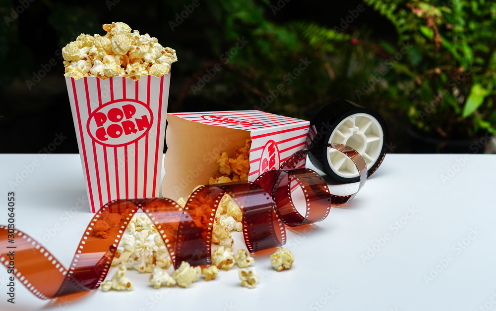A box of popcorn with a stip of 35mm film on a nature black background ...