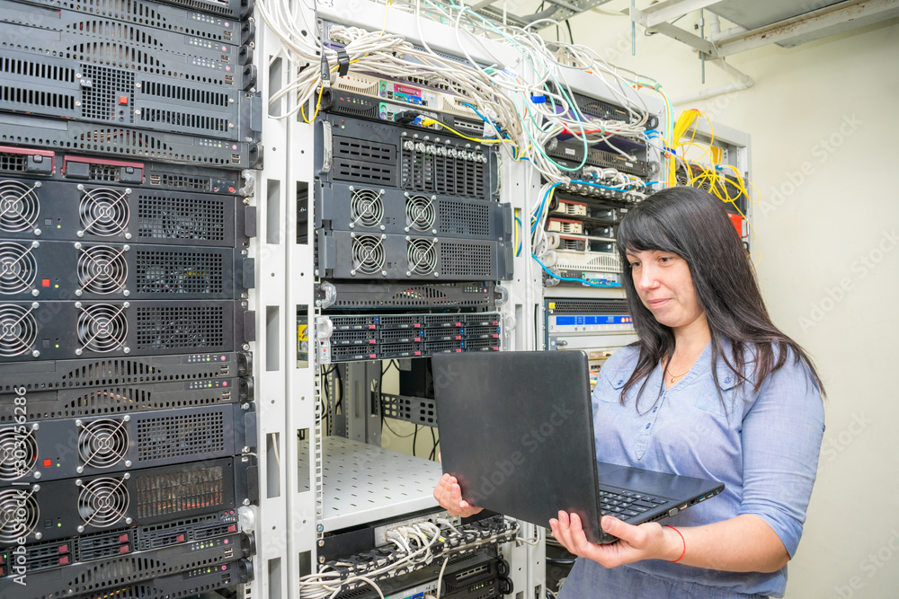 The girl programmer stands near the racks with computer equipment ...