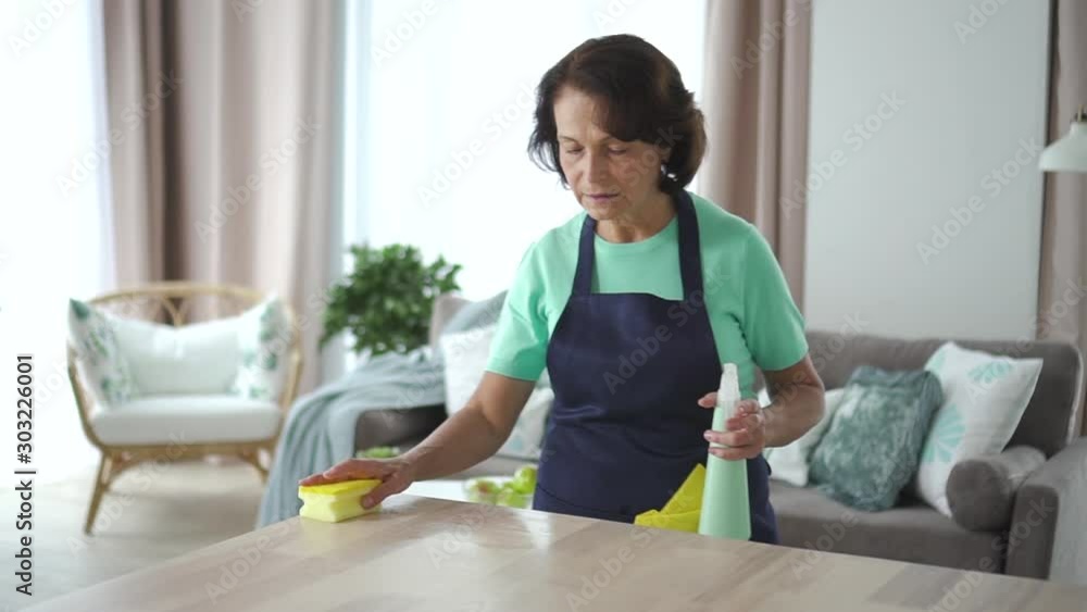 60s Elderly american woman housekeeper wipe table working in home room ...