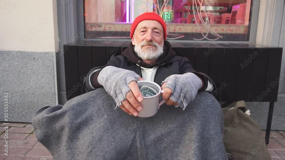 Homeless man in old clothes sitting on cardboard box asking for money ...