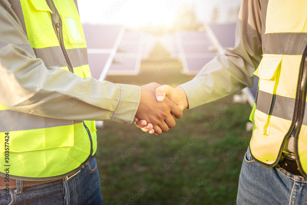 two asian male engineer wearing safety vest handshake with solar panels ...