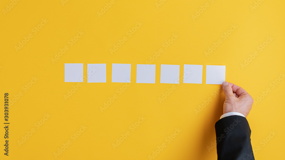 Hand of a businessman placing seven blank white post it papers in a row ...