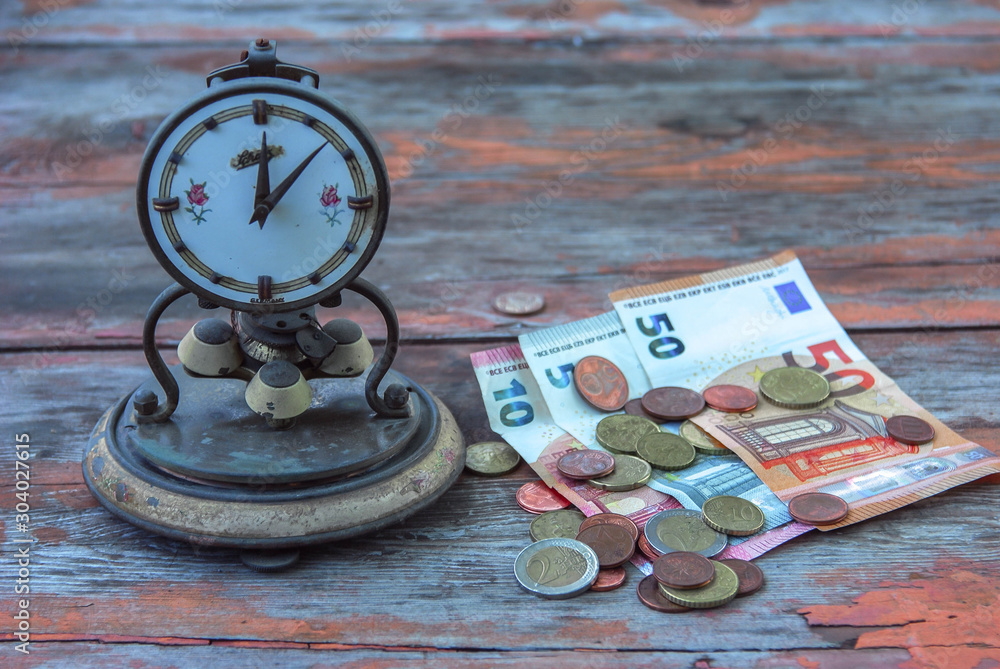 time is money concept. Antique clock, stand on an old table, next to ...
