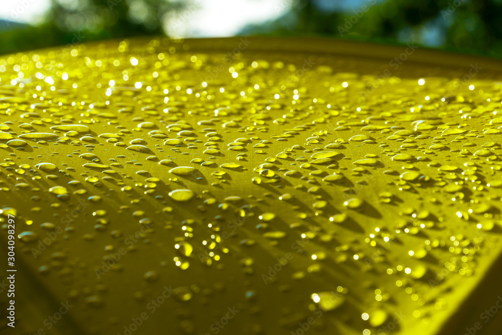 Rain drops on a yellow tourist tent in the morning sun. The material is ...