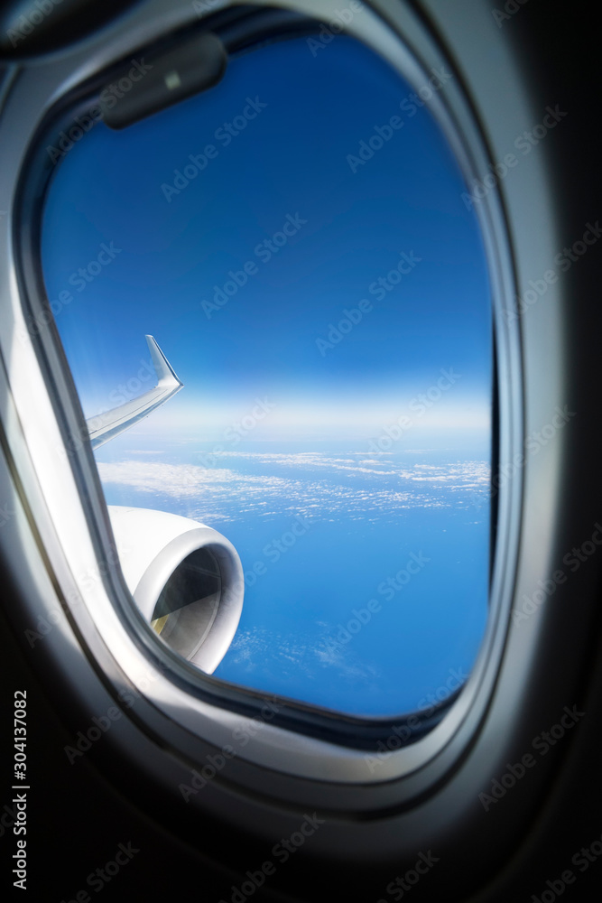 commercial airplane window with plane wing, engine, blue sky and clouds ...