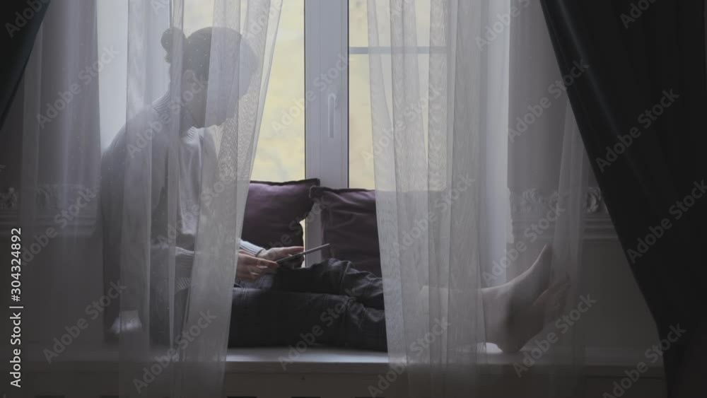 Girl sitting near the window uses a computer tablet. Monitor glows ...