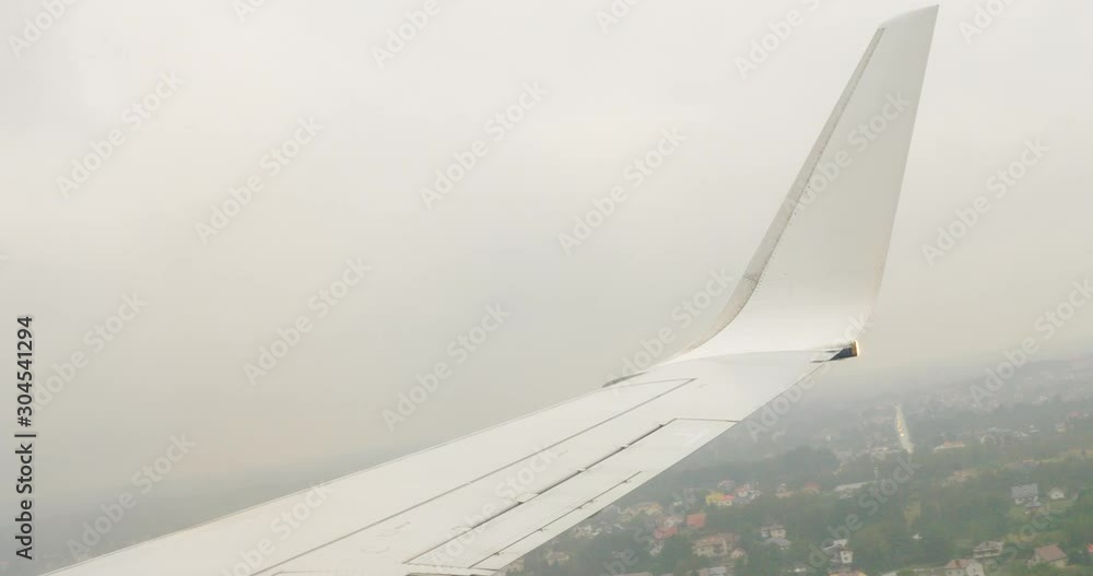 Plane landing through clouds of bad weather. View white wing through an ...