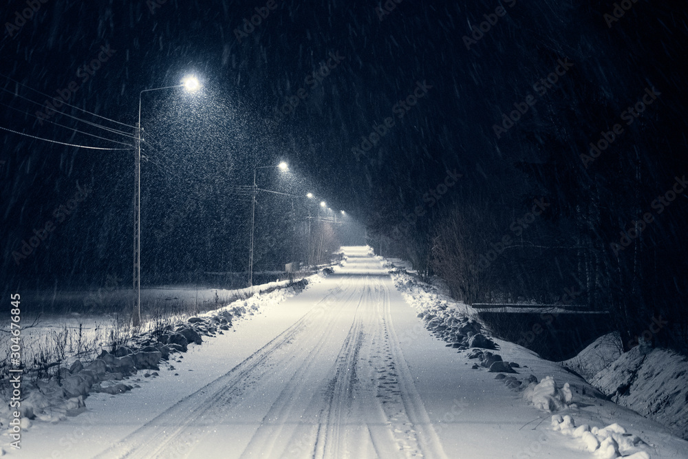 road in the blizzard snow in winter at night. In the light of lamps ...