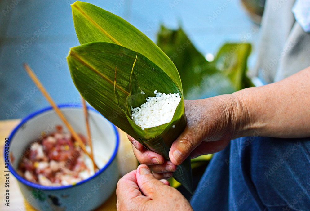 Hand holding leaf filled by sticky rice to make zongzi, traditional ...