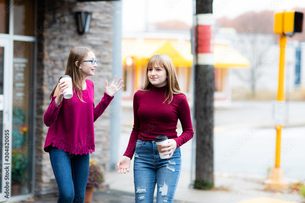 Two young teenager girls going from coffee store. Sisters talking and ...