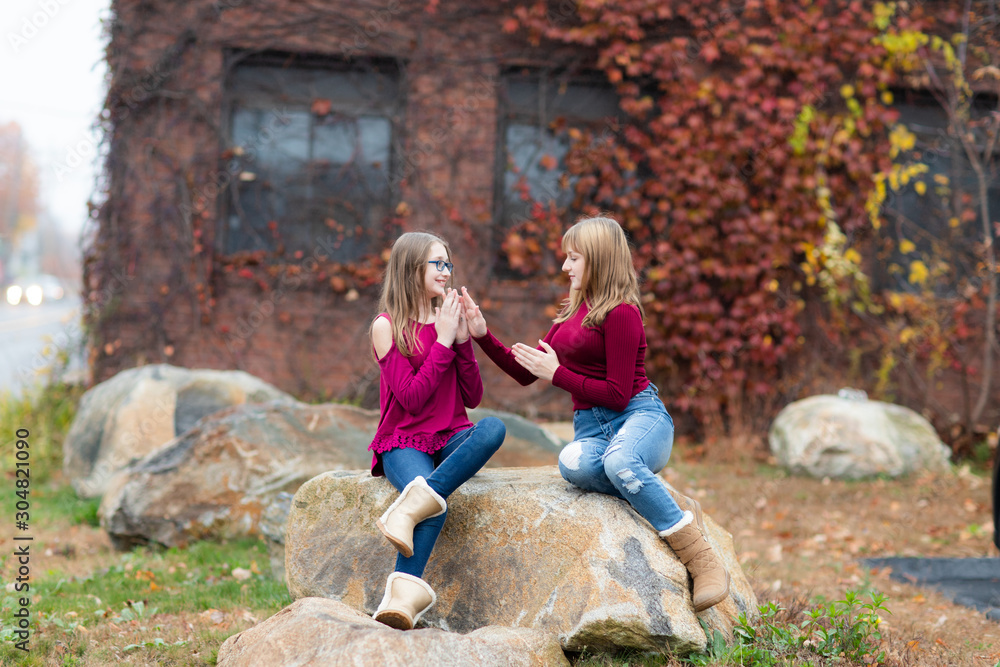 Two young teenager girls sitting on the rock. Sisters, friends happy ...